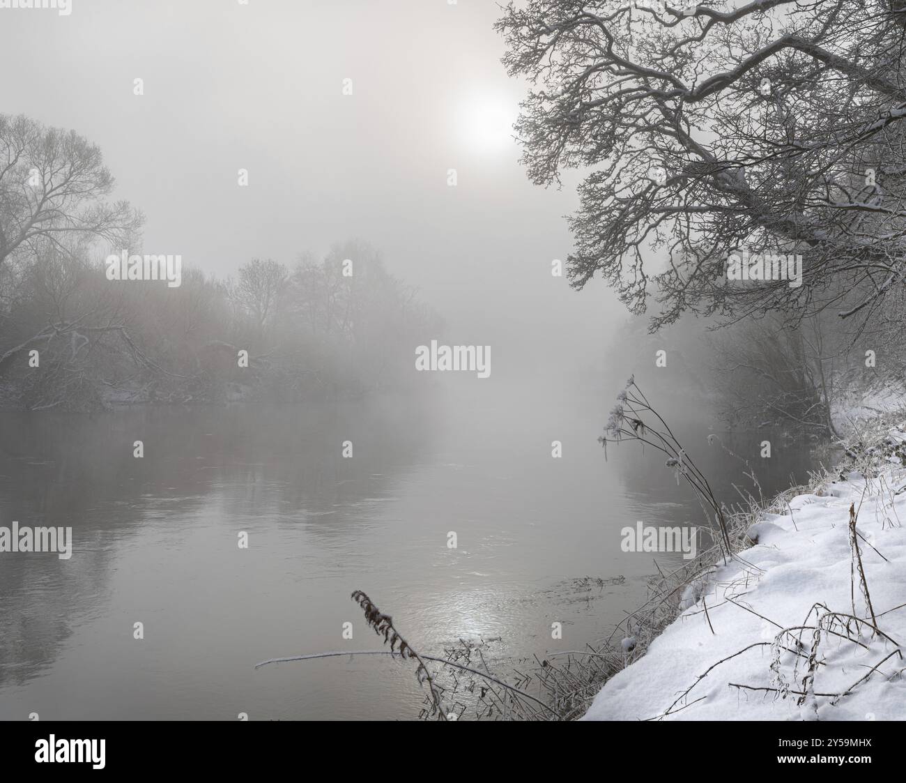 Sun breaking through the mist over the Teviot River in winter snow in ...