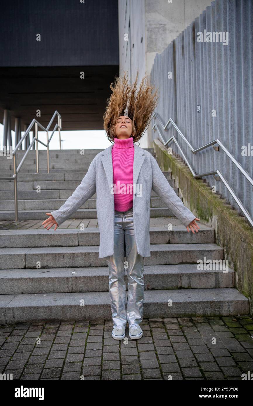 Young woman in stylish outfit flipping hair on urban stairs Stock Photo ...