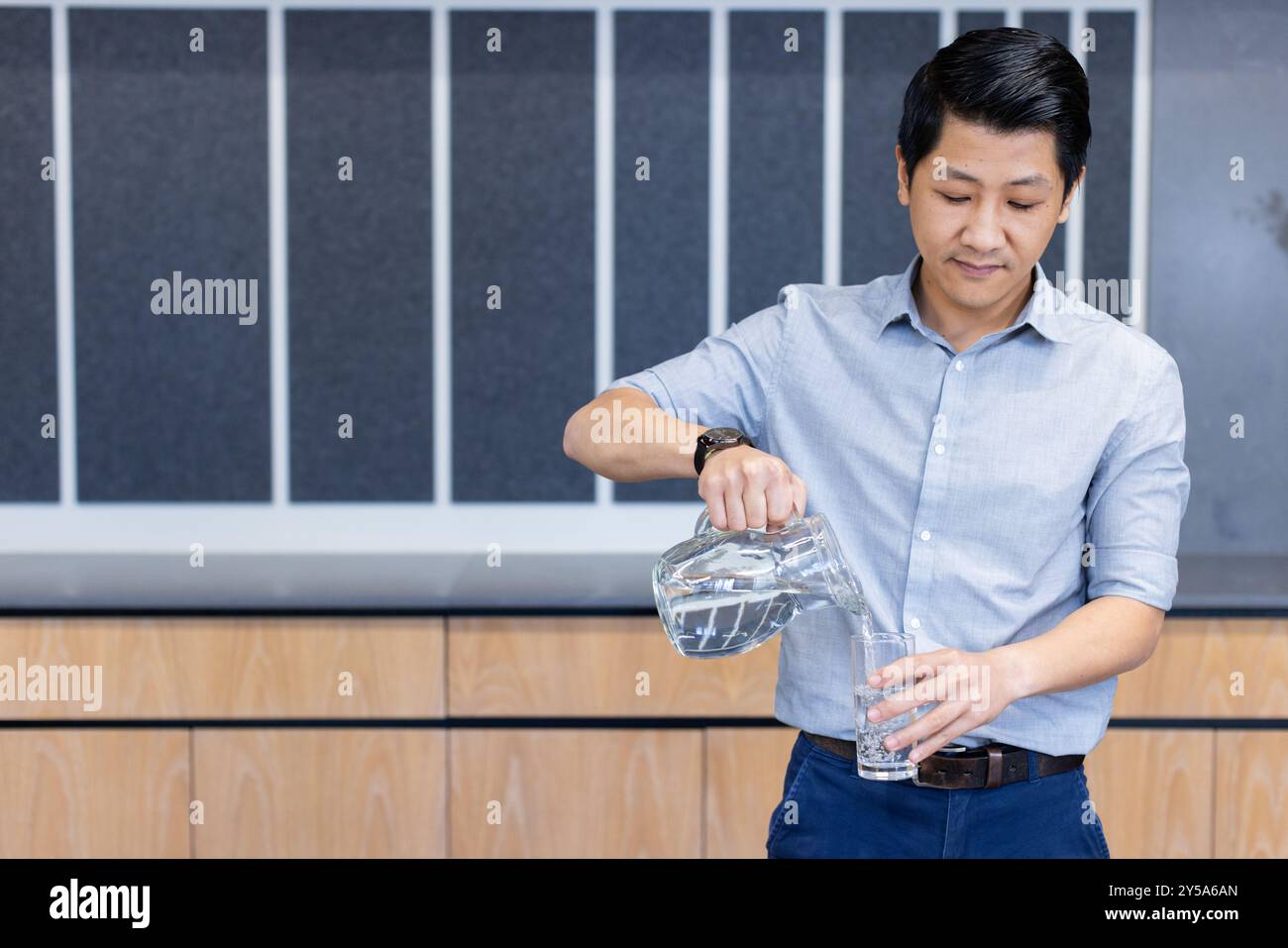 Pouring water from pitcher into glass, Asian man in business attire ...