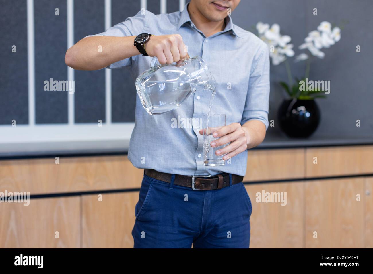 Pouring water from glass pitcher, Asian man in business attire ...