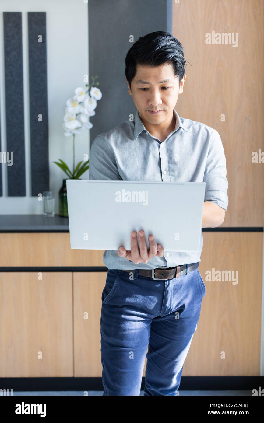 Working in modern office, asian man holding laptop and focusing on task ...