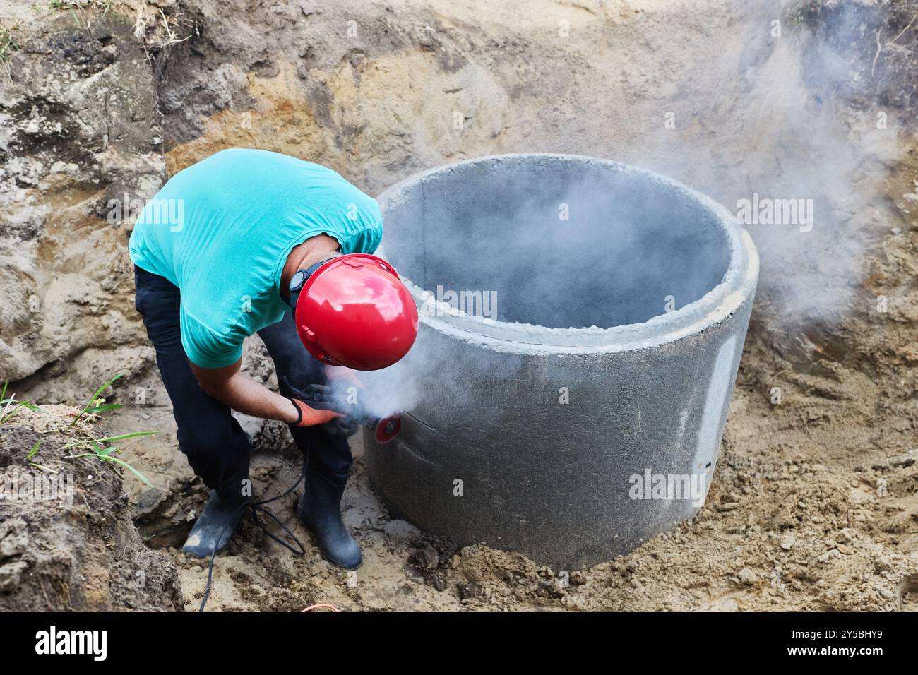 Worker makes hole for an inlet pipe in concrete septic tank ring using ...