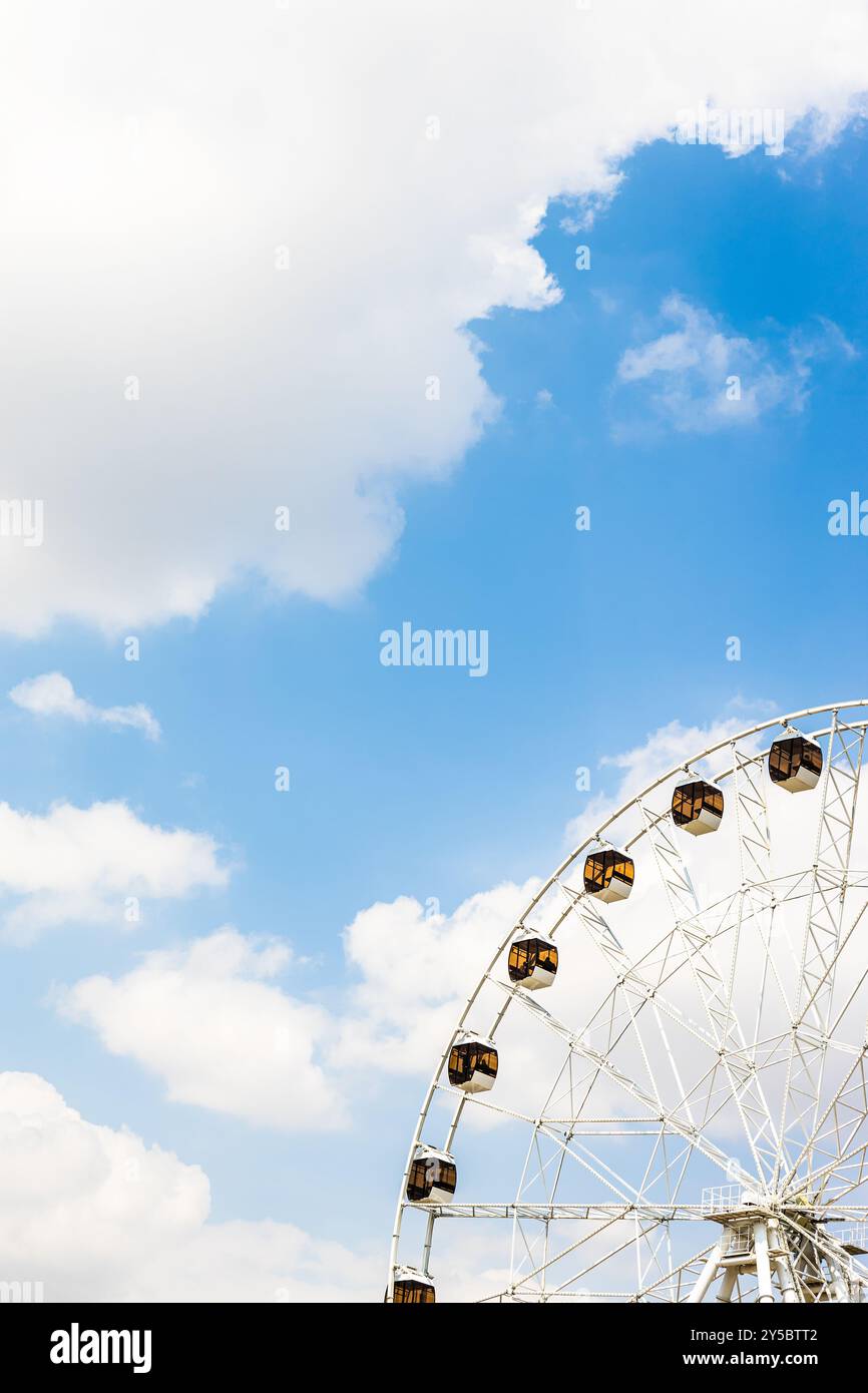 white observation wheel and white clouds in blue sky in background in ...