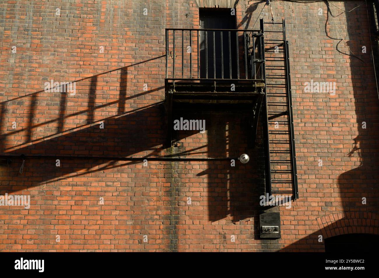 The shadow of the fire escape is cast onto a brick wall. Archer Street ...