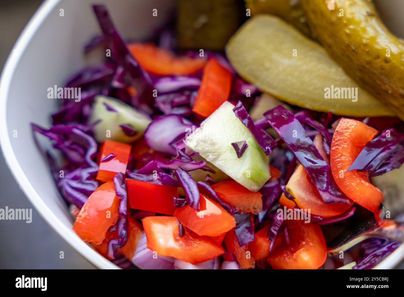 A bowl of vegetables with a pickle on top. The vegetables are red and ...