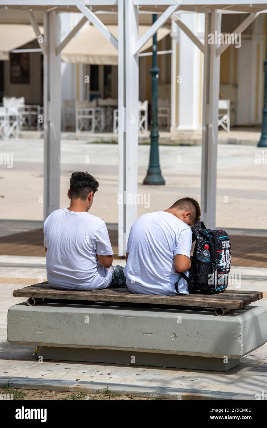 two young boys sitting together on a wall using their smartphones, two ...