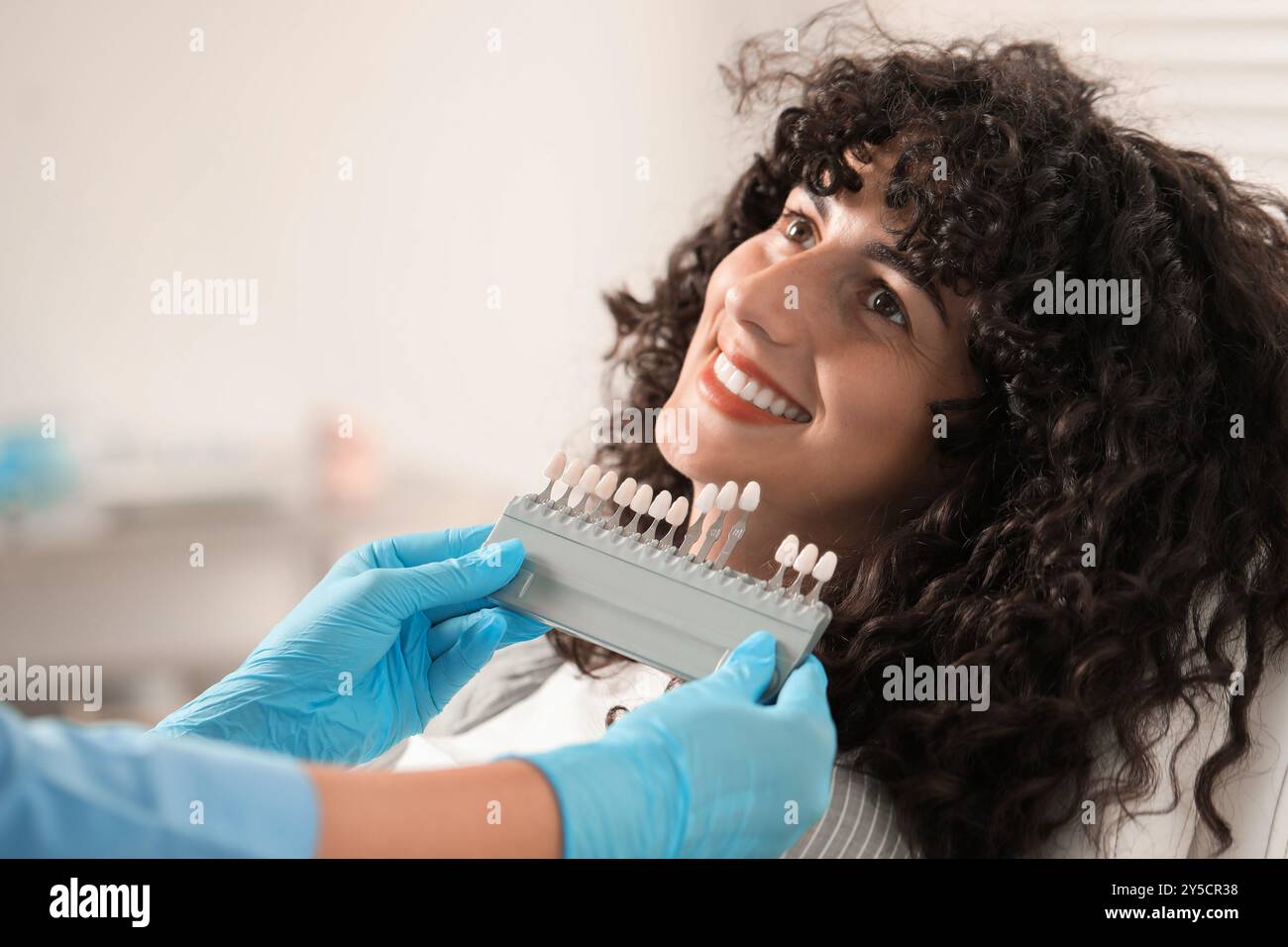 Doctor checking young woman's teeth color in clinic, closeup. Dental ...