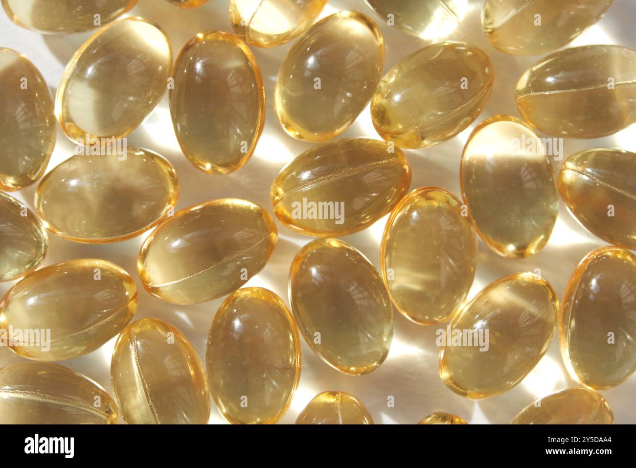 Close-up of translucent gel capsules with golden hue reflecting ...