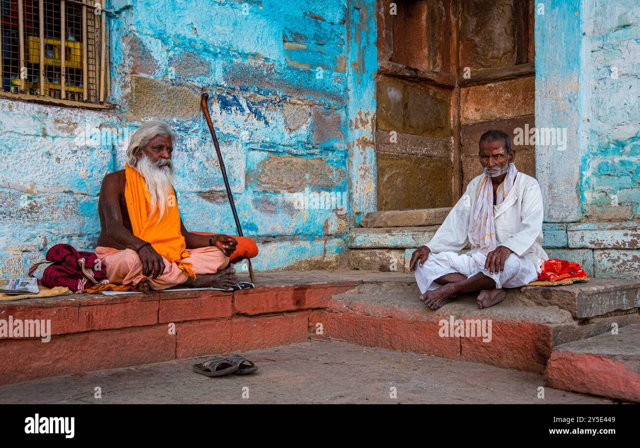 Two indian men sitting and resting in front of a colorful building ...