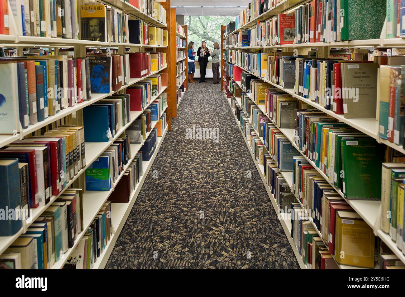Three women stand at end of row of books in library using sign language ...