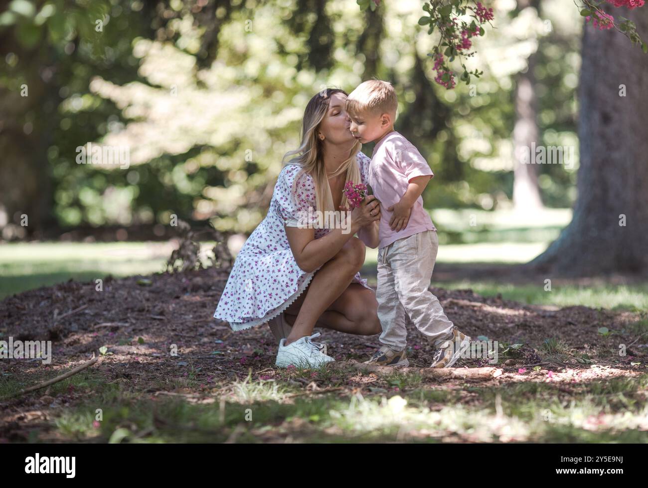 A mother woman kisses a baby boy on the cheek while walking in nature ...