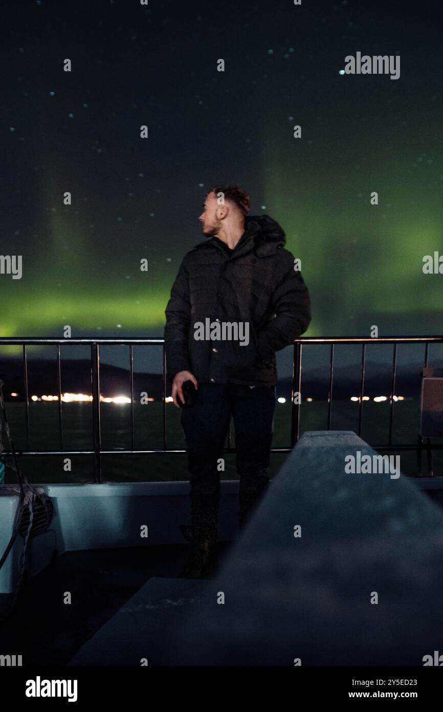 Man on back of cruise ship in front of strong northern lights in Tromso ...