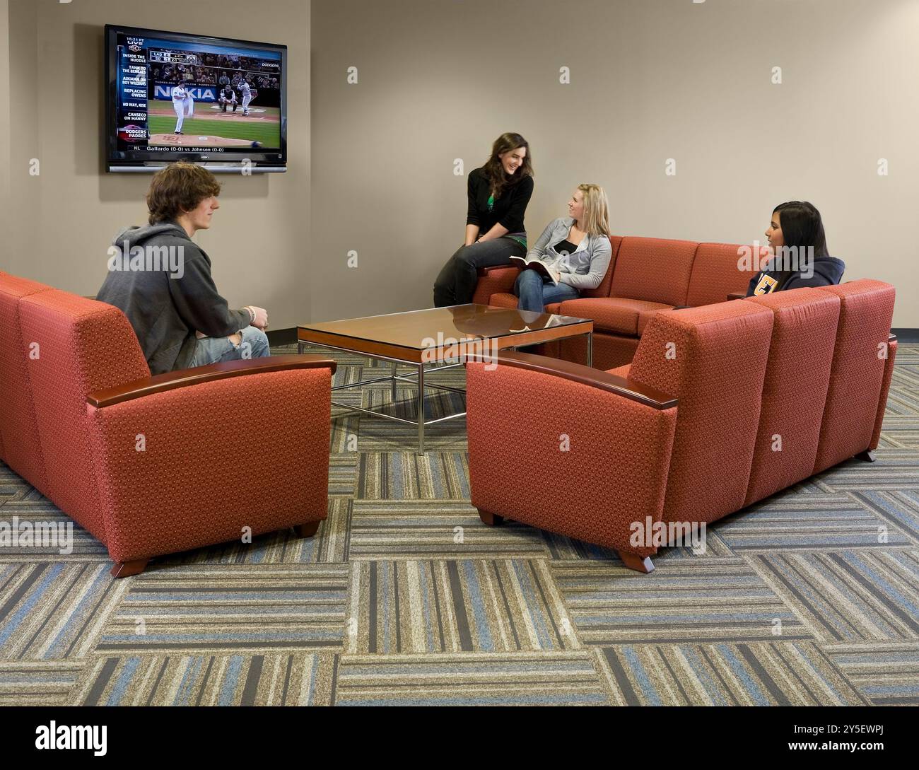 Four students sit and talk in lounge with television on the wall Stock ...