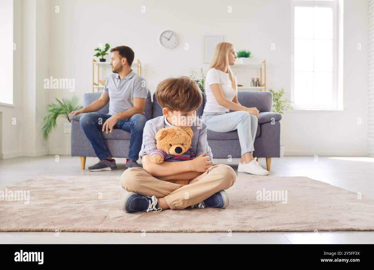 Upset boy sitting on floor while his mother and father ignoring each ...