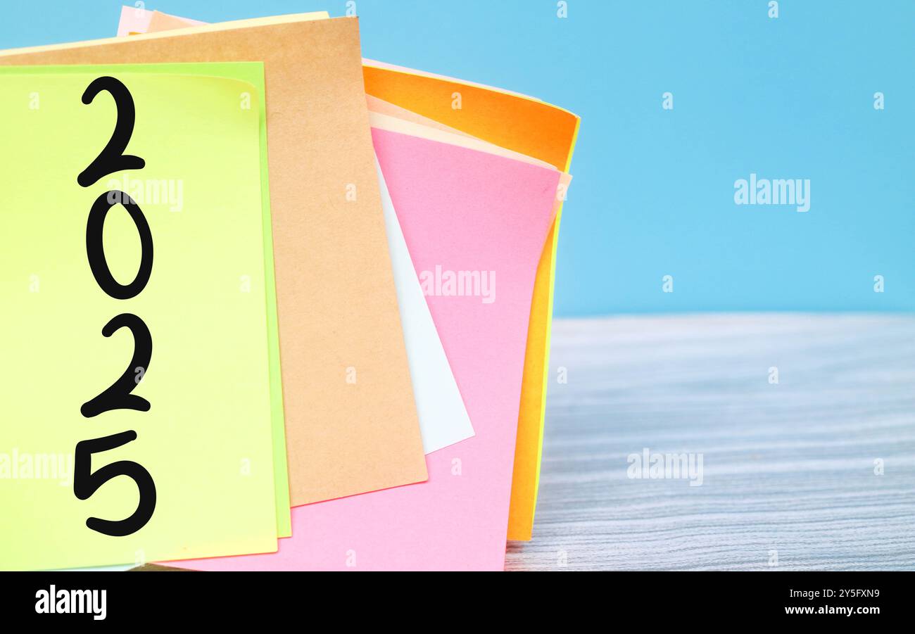 2025 written on sticky note attached to the wall isolated on blue ...