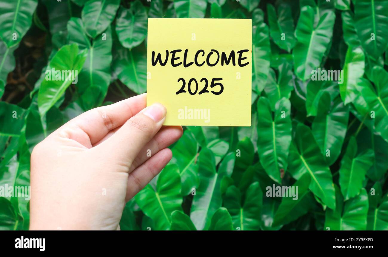 Hand holding a note Welcome 2025 with a plant background. New year ...