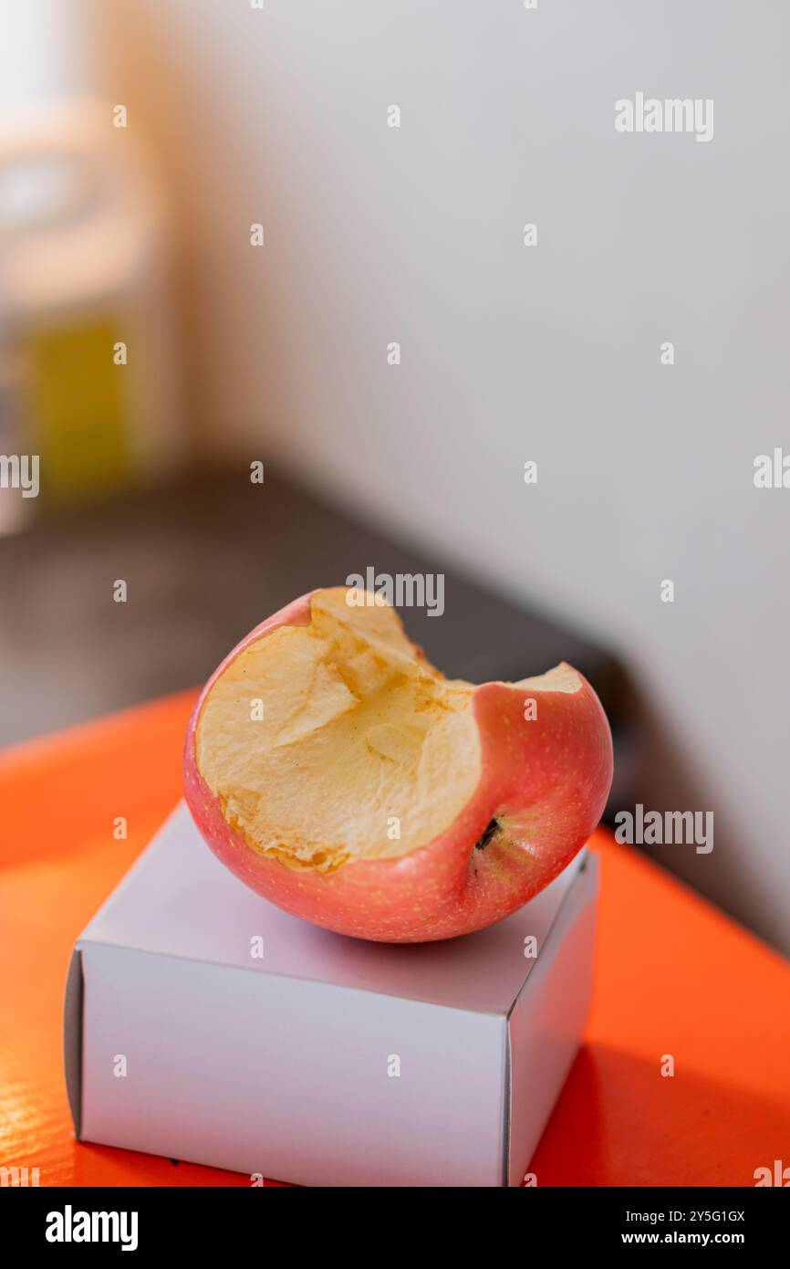 A bitten red apple resting on a small white box. The apple has a shiny ...
