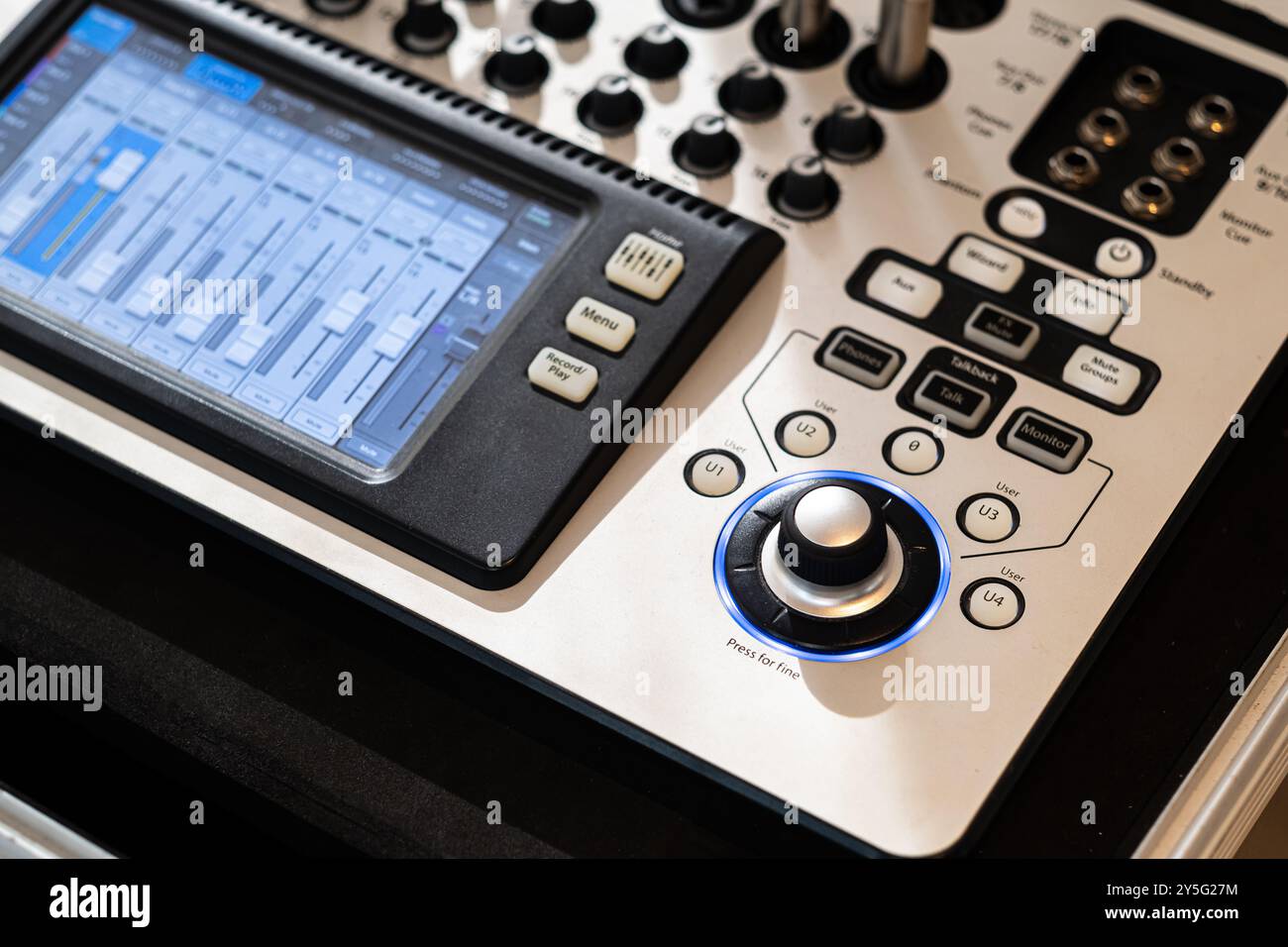 A close-up view of a modern audio mixing console featuring various knobs, buttons, and a digital ...