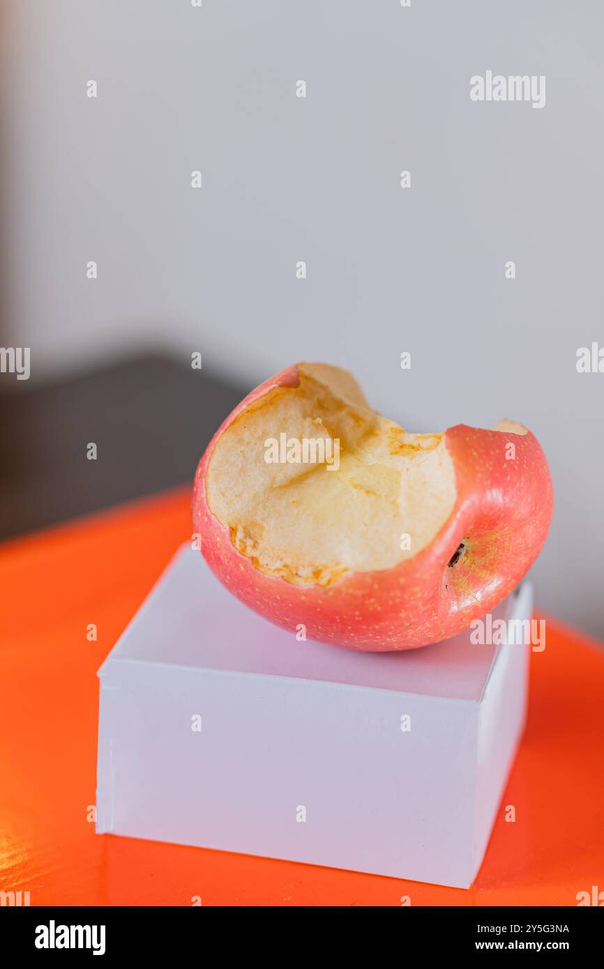A bitten apple resting on a small white box with an orange surface. The ...
