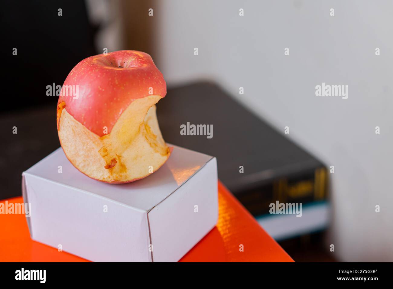 A partially eaten red apple resting on a small white box. The apple has ...