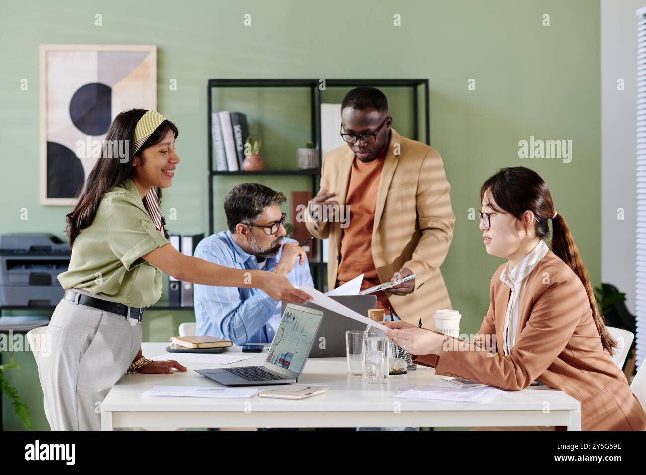 Team collaborating during office meeting, sharing ideas and discussing projects around desk ...