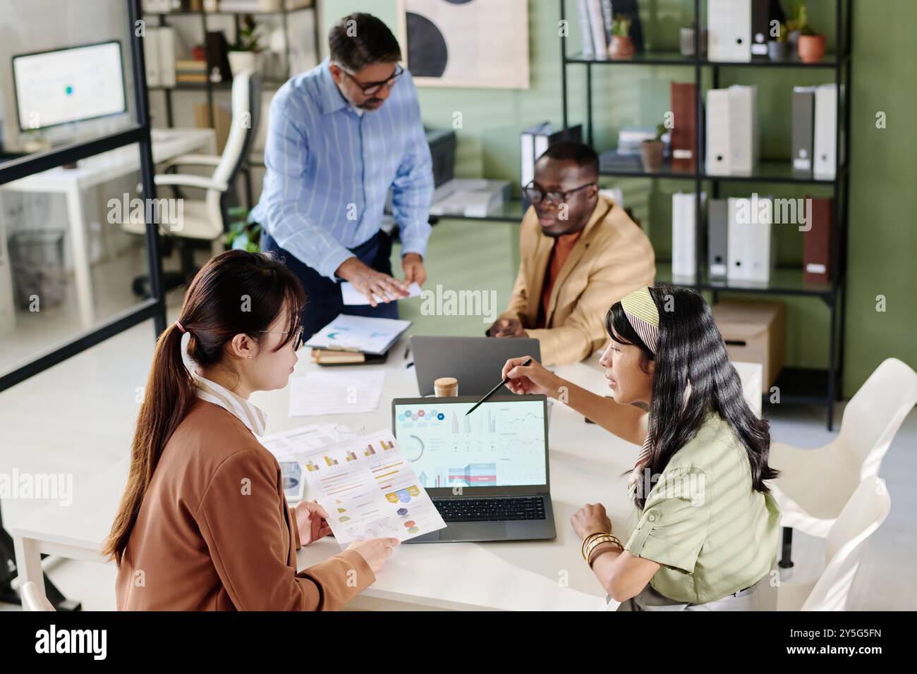 Group of co-workers interacting in modern office with open laptops on ...