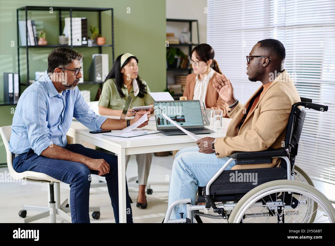 Group sitting around table in office discussing strategies while one ...