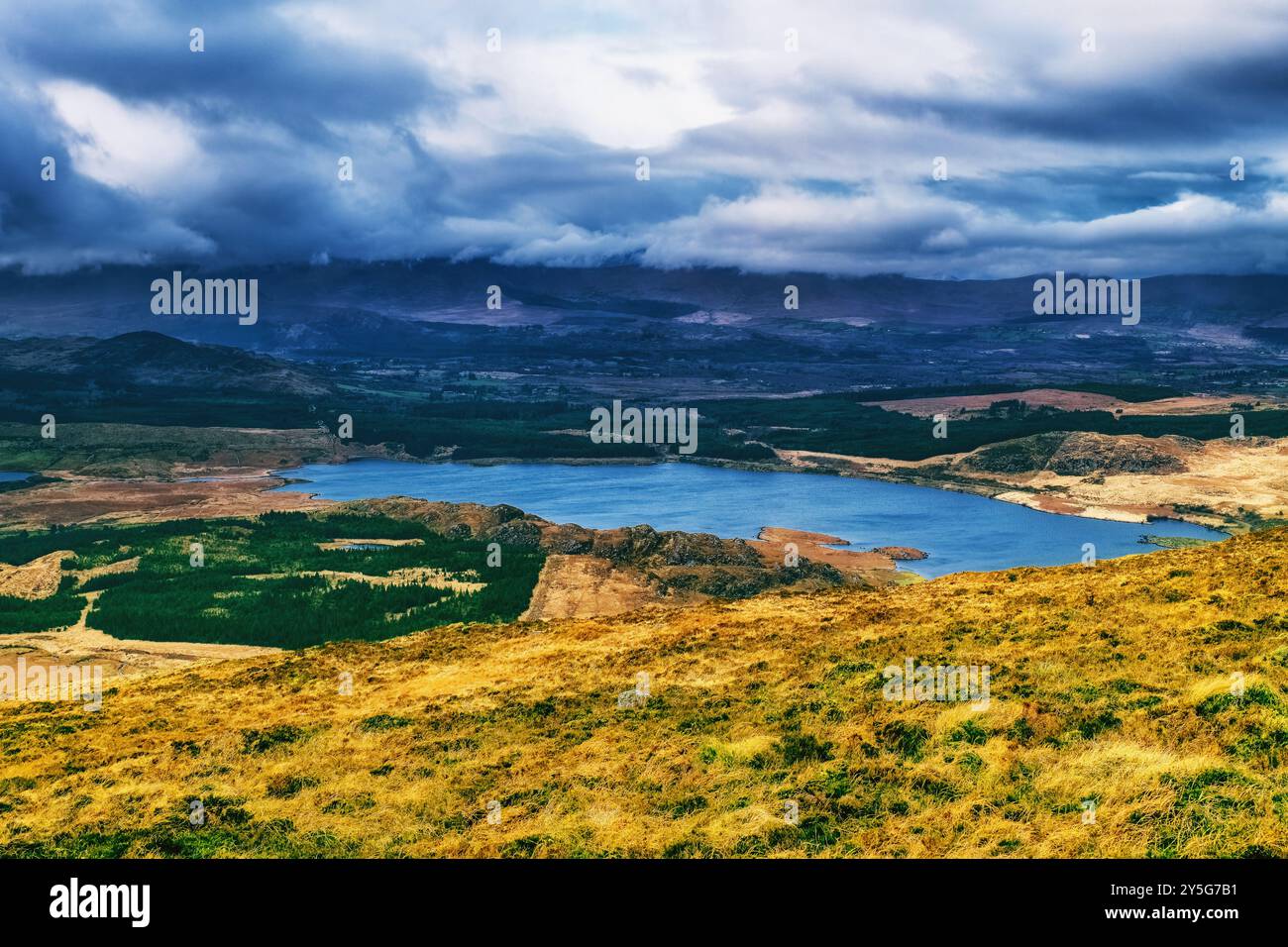 A panoramic view of a lake nestled between hills, with a blue sky and a ...