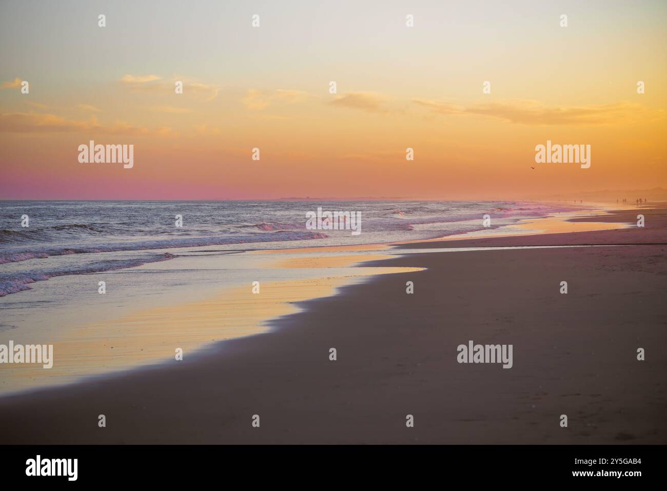 Sunset casts a warm glow over the serene beach scene Stock Photo - Alamy