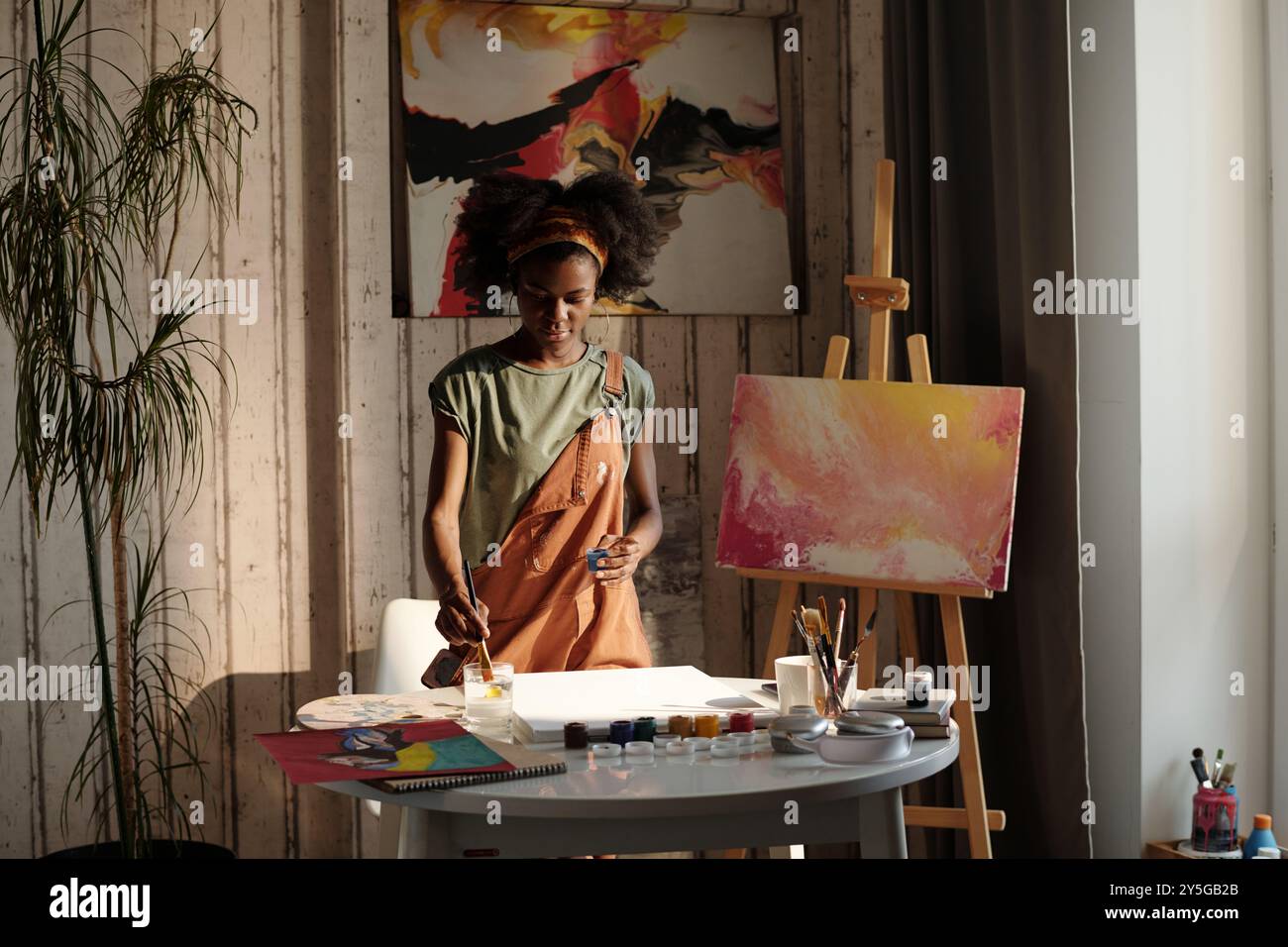 Black person artist, surrounded by paintings, working in cozy home ...