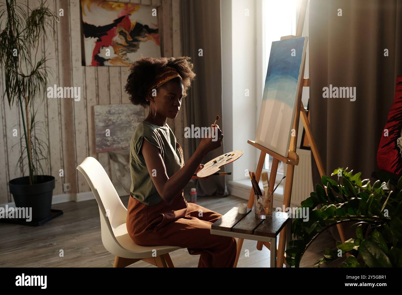 Young artist surrounded by art supplies, creating painting on canvas in ...