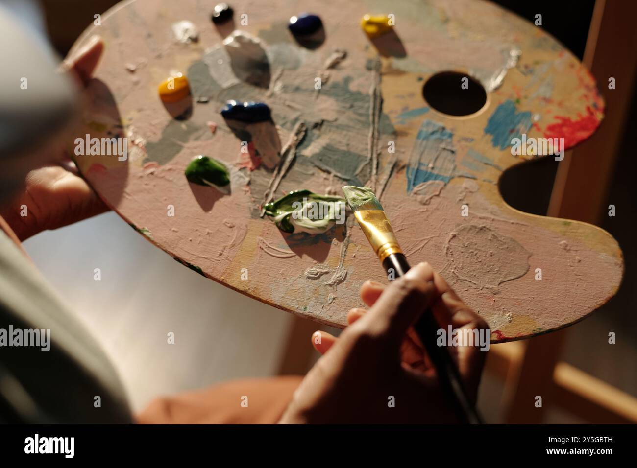 Hand holding paintbrush mixing vibrant hues on a well-used paint ...