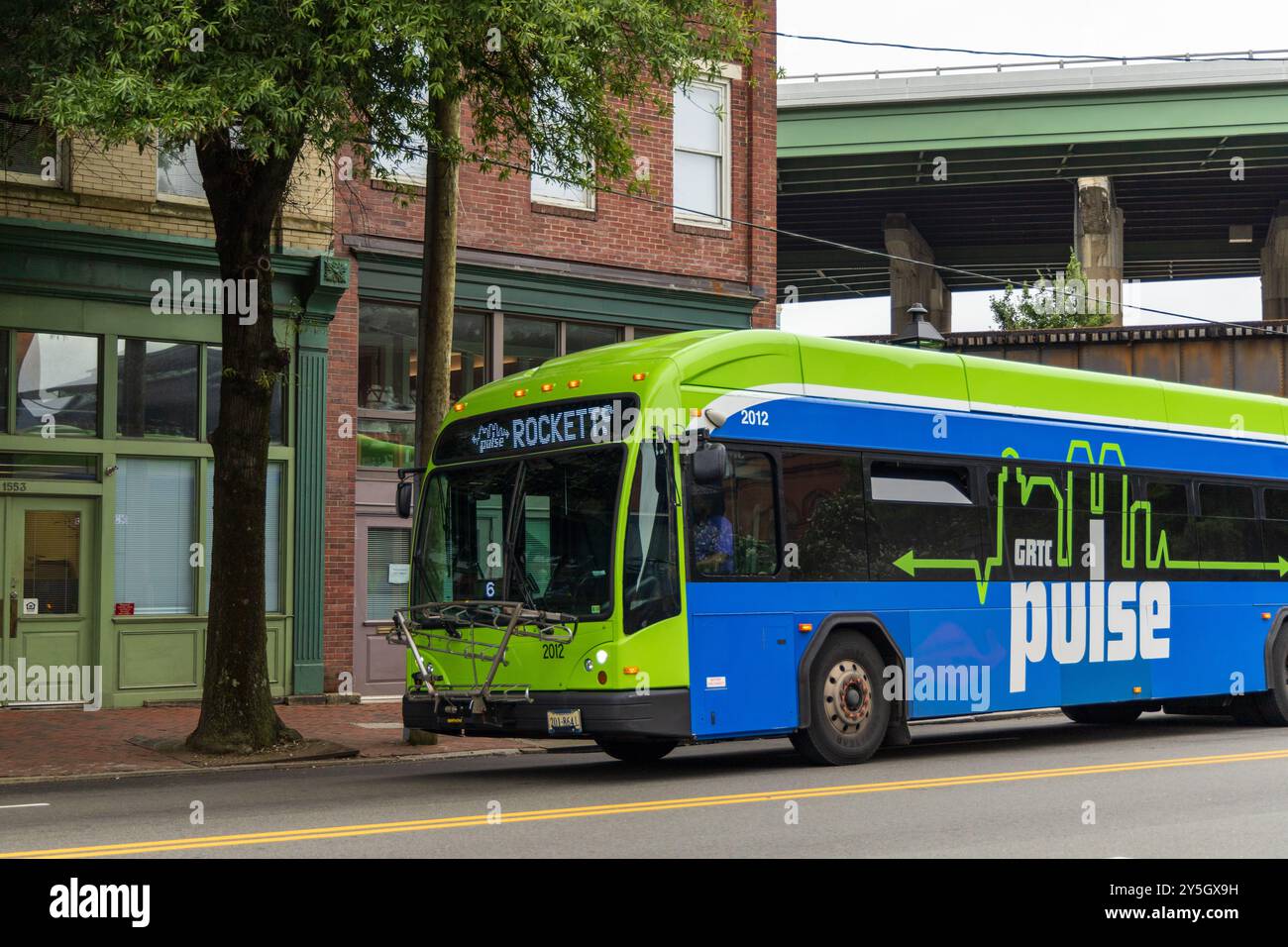 A green and blue bus is driving down a street. The bus is labeled with ...