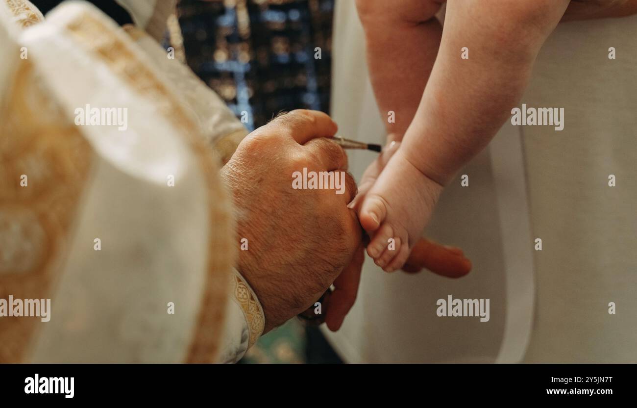 A priest anoints a baby's feet with oil during a traditional Christian ...