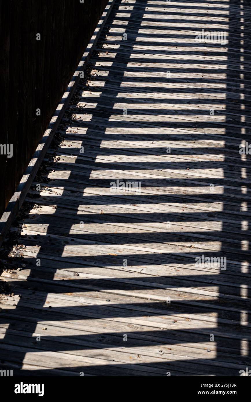 A wooden walkway with a shadow cast on it. The shadow is long and ...