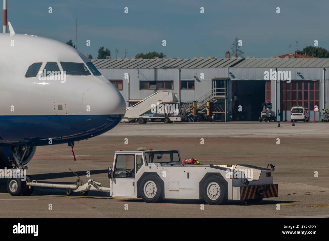 A white pushback tug pushes a plane inside the airport, Pisa, Italy ...