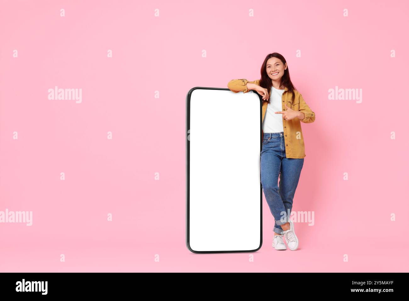 Happy smiling woman pointing at big mobile phone with blank screen on ...