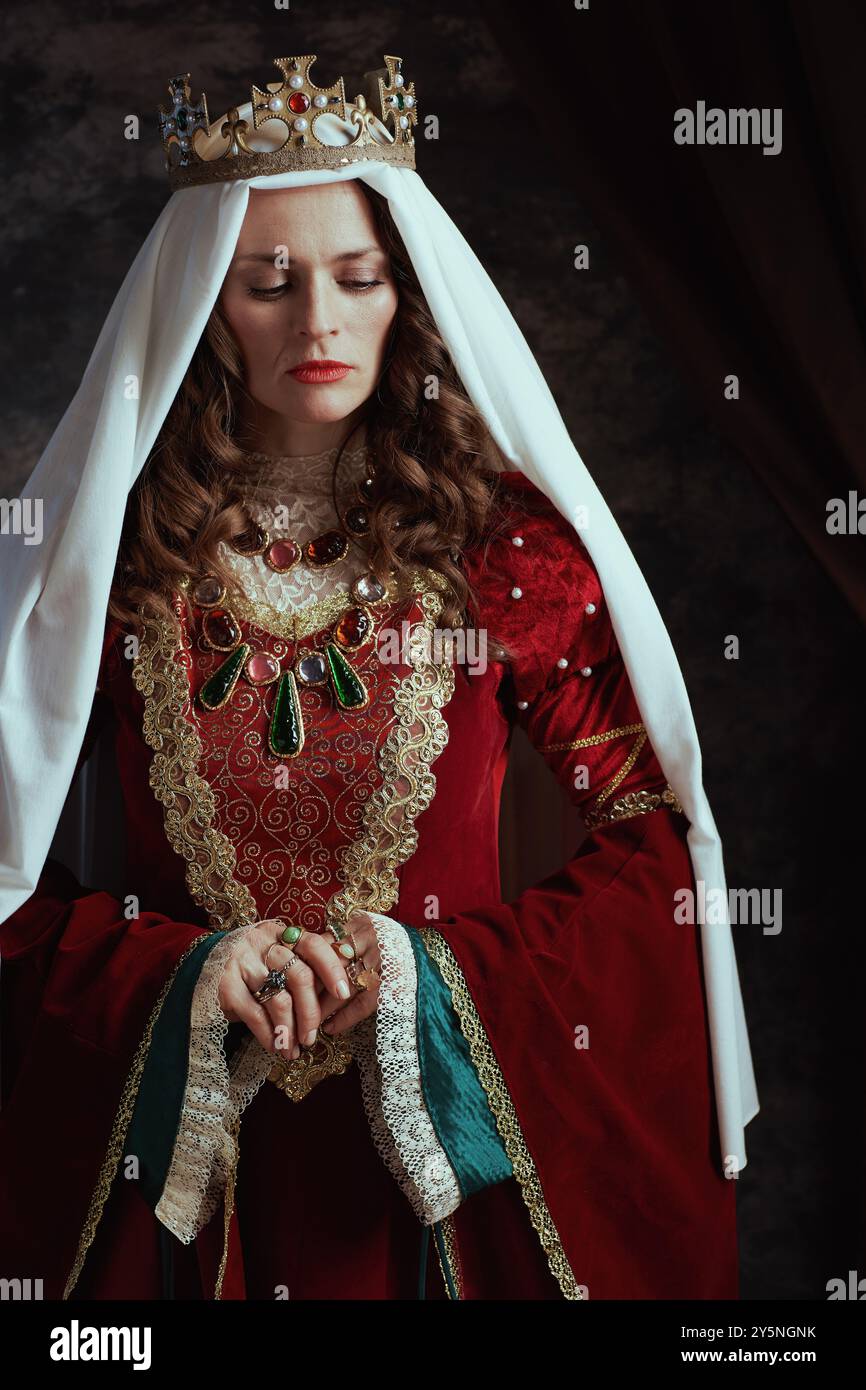 medieval queen in red dress with veil and crown on dark gray background ...