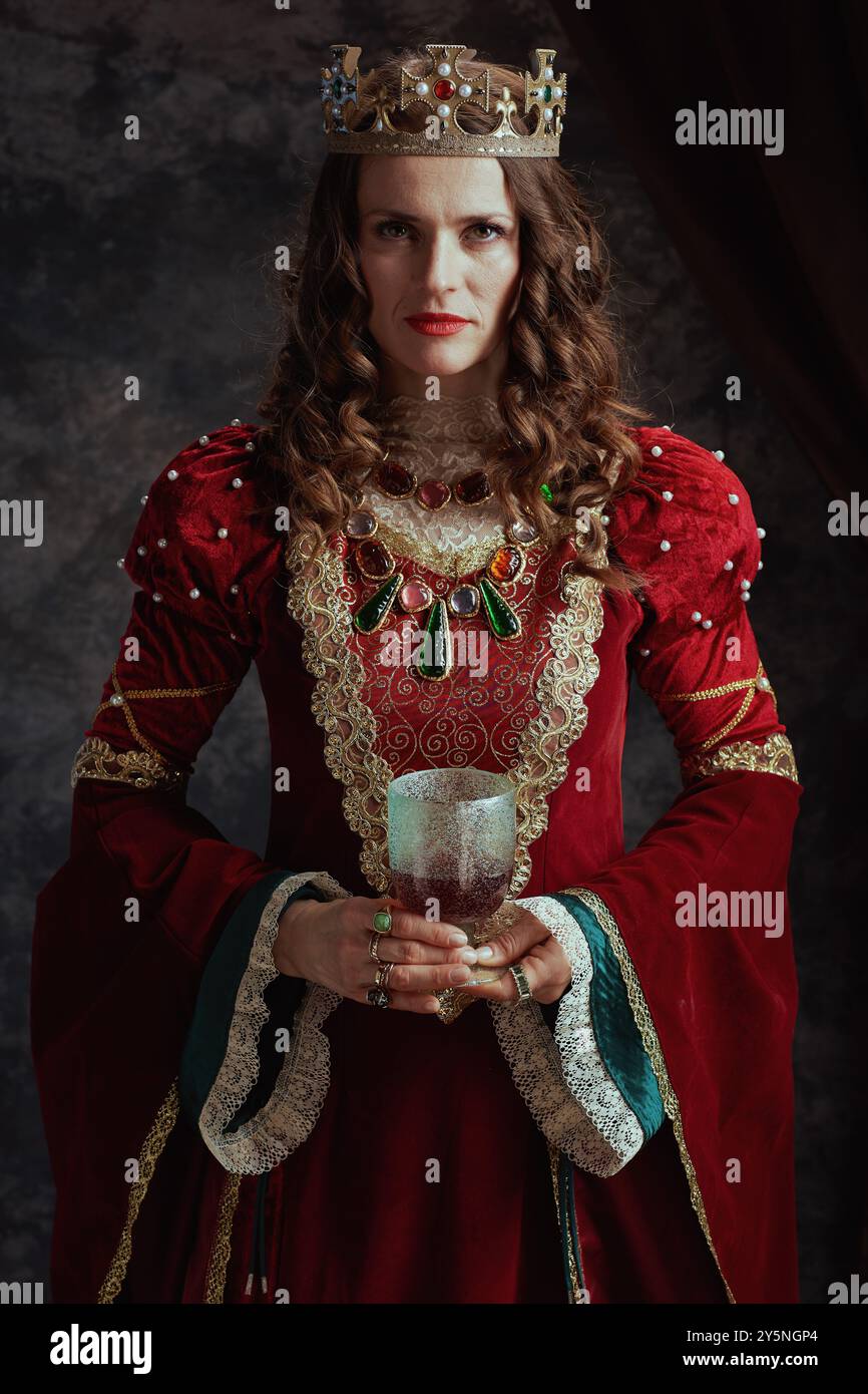 medieval queen in red dress with goblet and crown on dark gray ...
