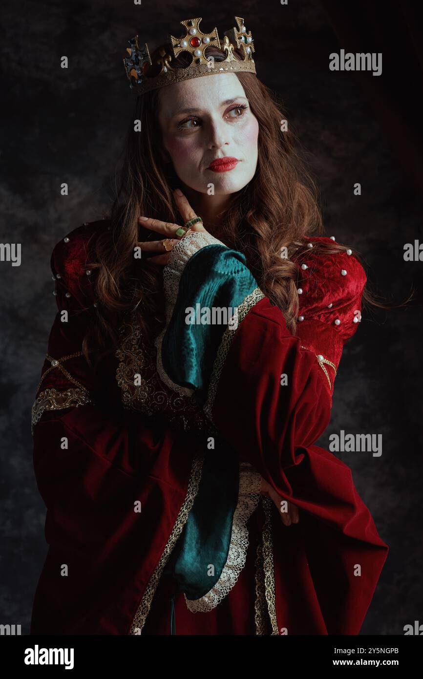 medieval queen in red dress with white makeup and crown on dark gray ...