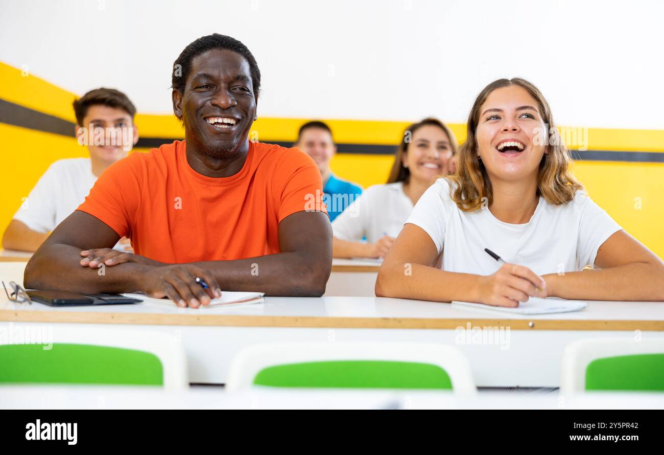 Cheerful smiling adult students at their desks in university classroom ...