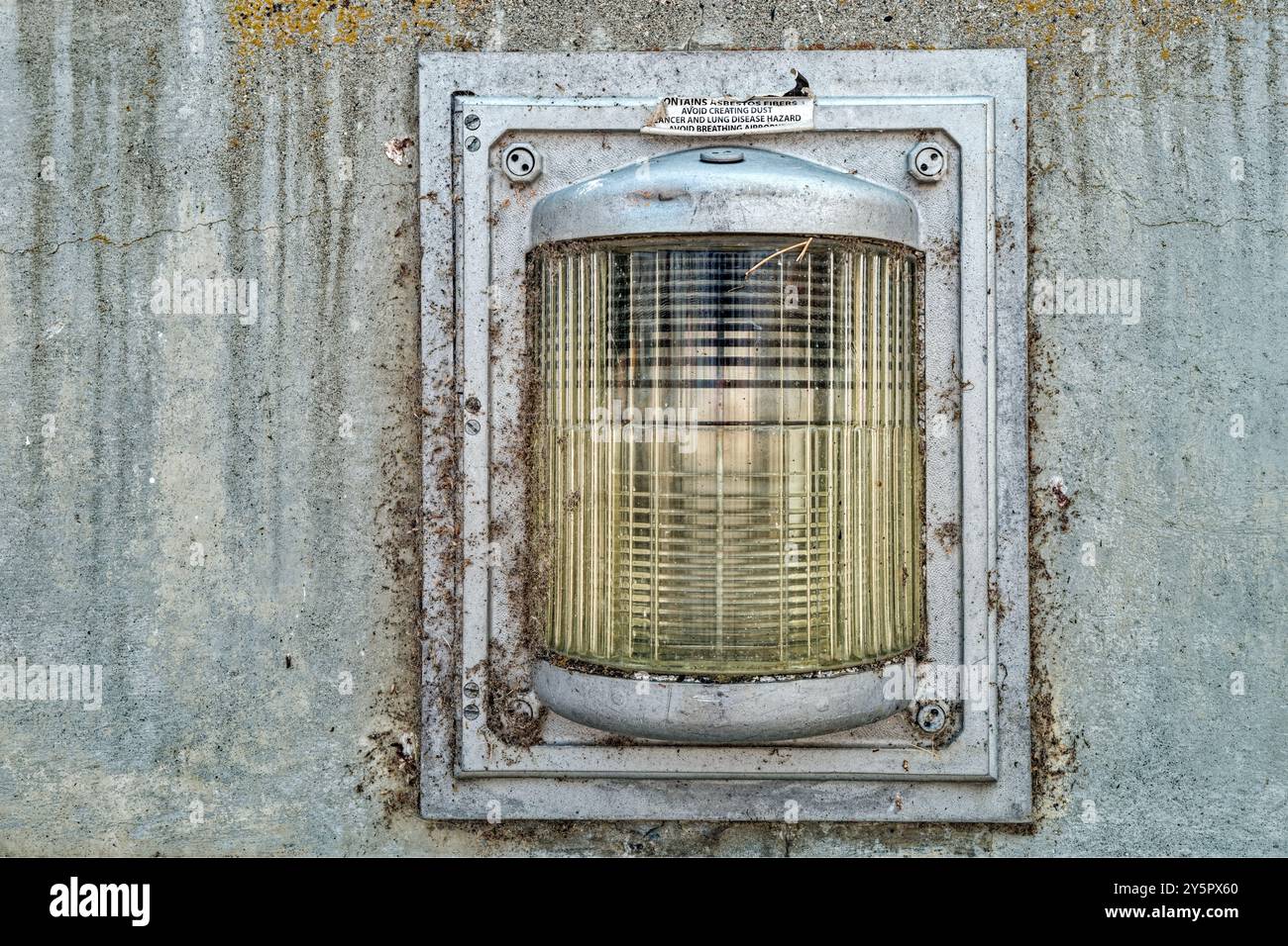 A dirty electric lamp with an asbestos warning is installed in the side ...