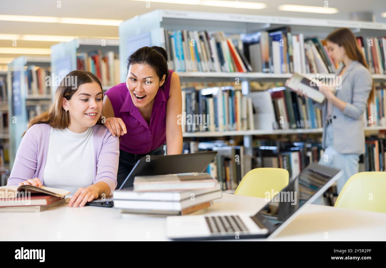 Two surprised female colleagues working on join project in library ...