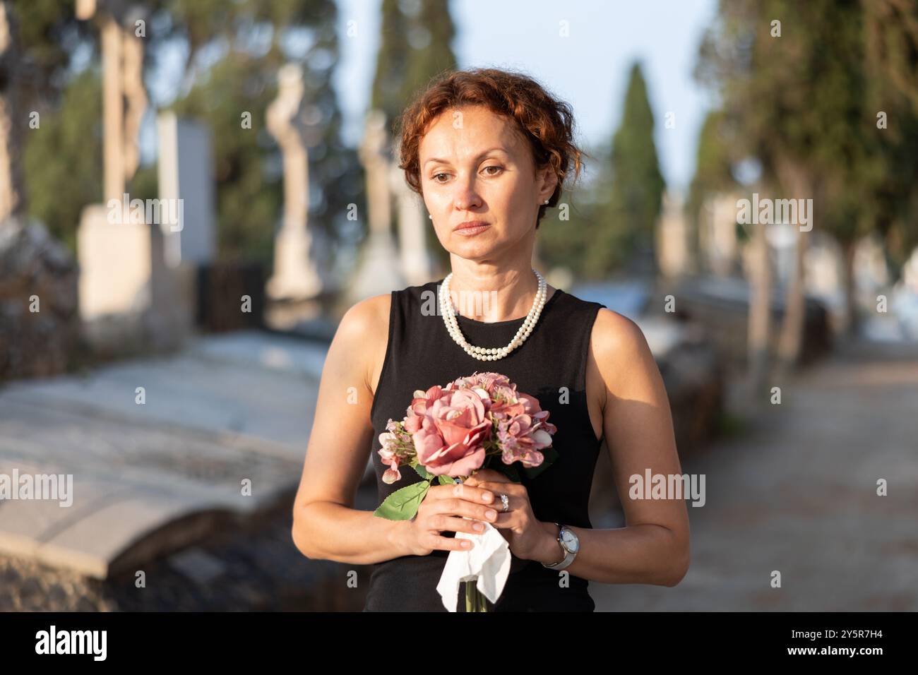 Grieving woman in black with flowers standing in cemetery Stock Photo ...