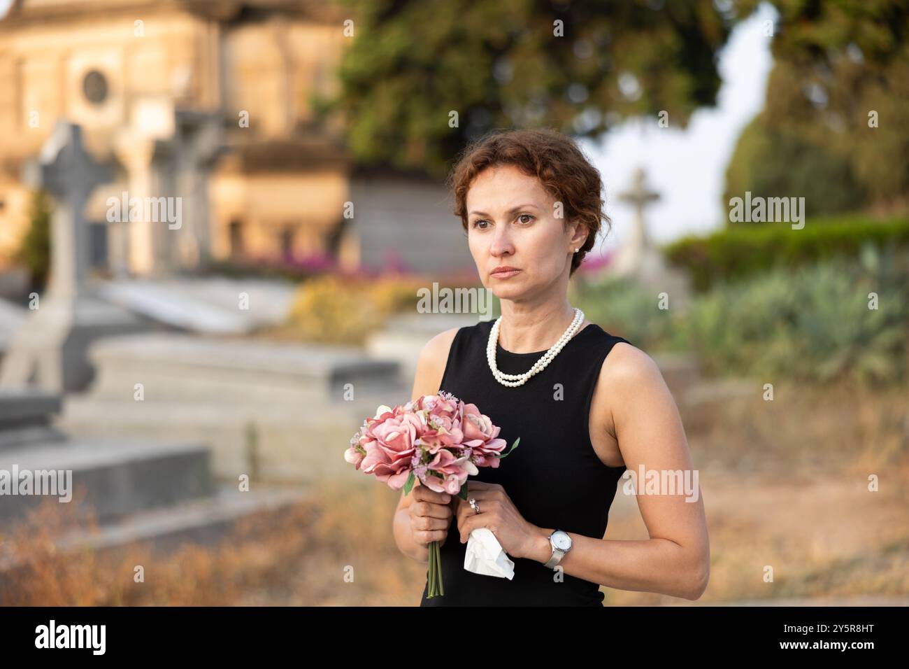 Grieving woman in black standing in cemetery with flowers Stock Photo ...