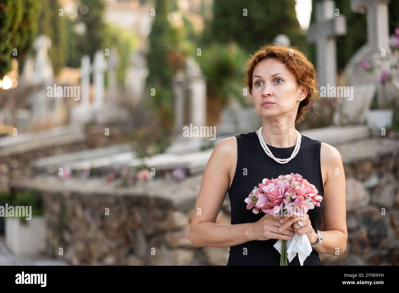 Upset woman in black dress, who lost loved one, brings flowers to grave ...