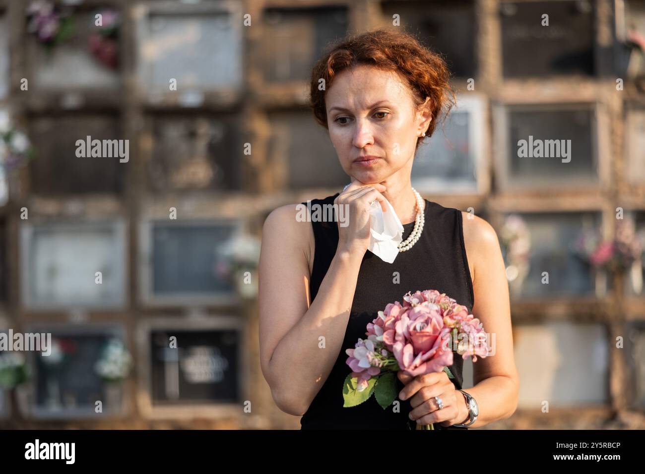 Woman in black mourning dress standing with flowers near columbarium ...