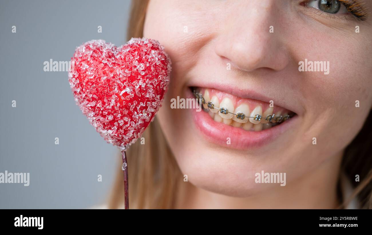 Cute woman with braces on her teeth holds a candy in the form of a ...