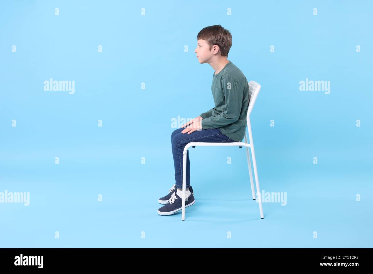 Boy with incorrect posture sitting on chair against light blue ...