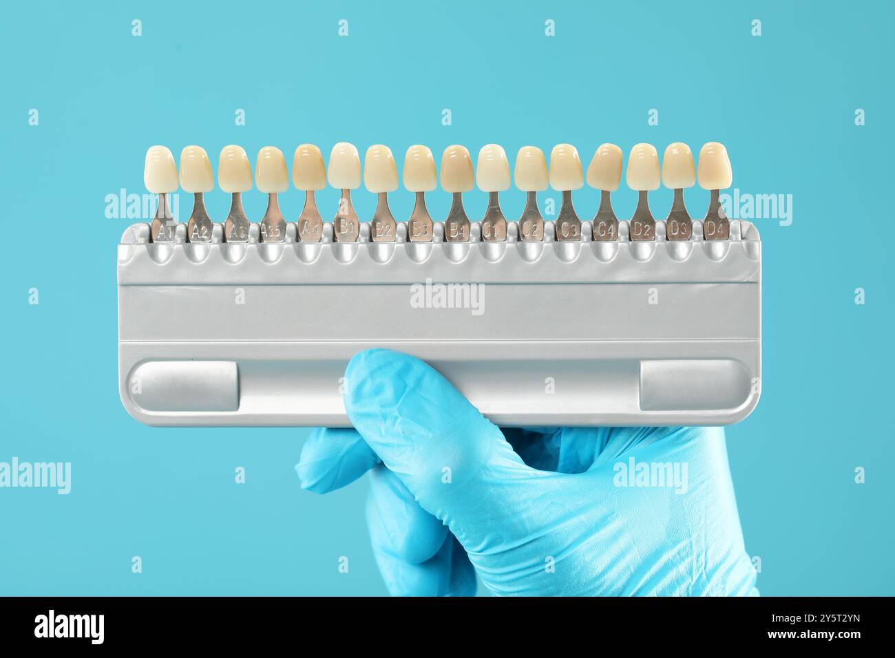 Doctor with teeth color chart on light blue background, closeup. Dental ...